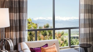 Quarto com grande janela e vista para as montanhas, sofá com almofadas, luminária e mesa pequena.