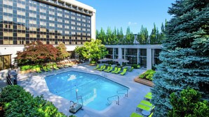 Um hotel com piscina, rodeado por cadeiras verdes e um edifício grande ao fundo.