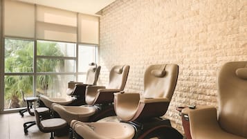 Quarto com várias cadeiras de massagem, parede de tijolos e grandes janelas com vista para palmeiras.