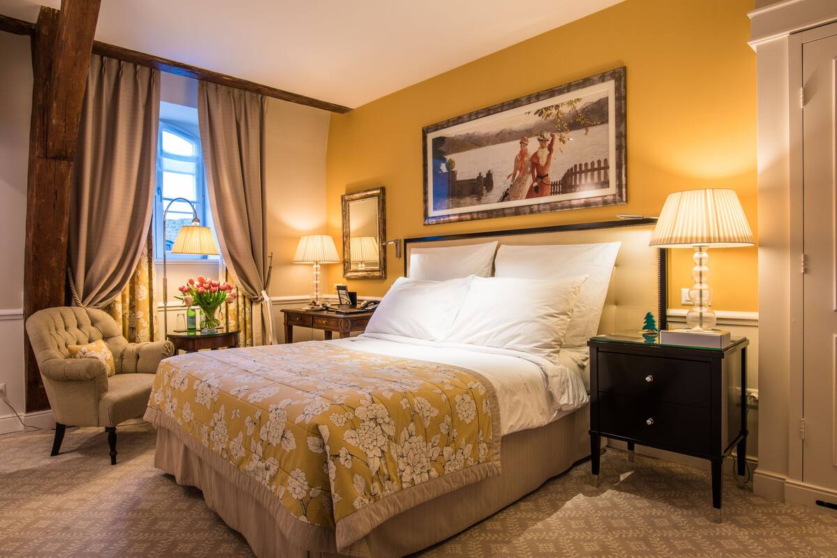 Quarto de hotel com uma cama grande, uma cadeira, uma mesa de cabeceira e um abajur.