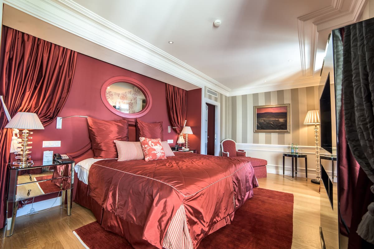 Um quarto espaçoso com uma cama grande, cortinas vermelhas, um espelho redondo e um quadro na parede.