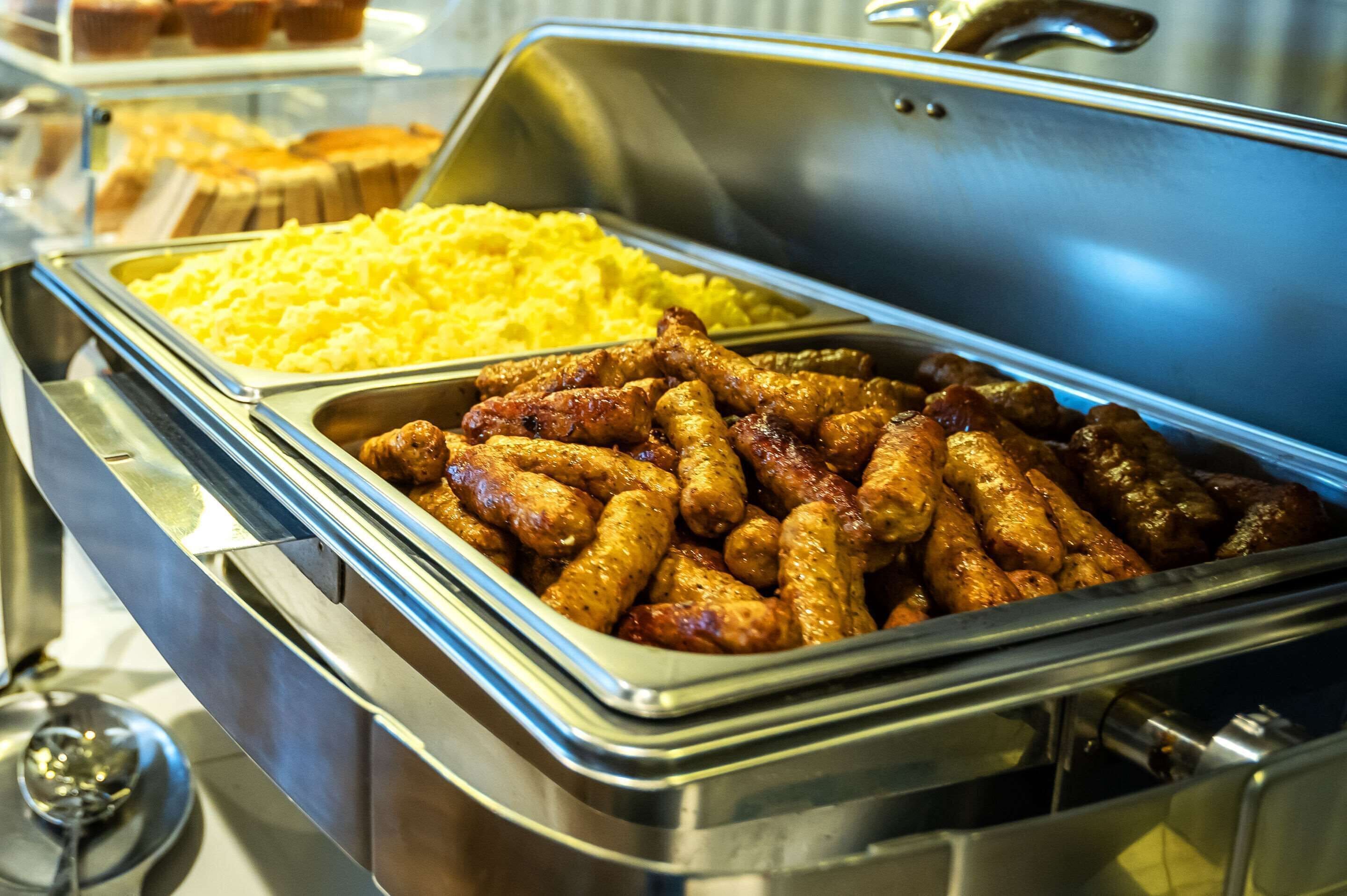 Buffet com diversas opções de comida, incluindo ovos mexidos e linguiça grelhada.