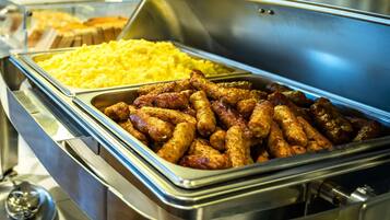 Buffet com diversas opções de comida, incluindo ovos mexidos e linguiça grelhada.