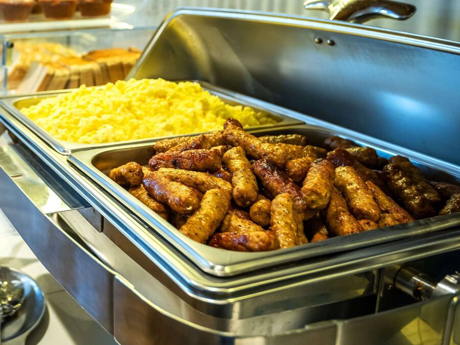 Buffet com diversas opções de comida, incluindo ovos mexidos e linguiça grelhada.