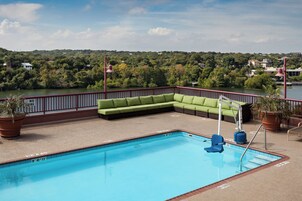 Área de piscina com um sofá verde e vista para um lago e casas ao longe.