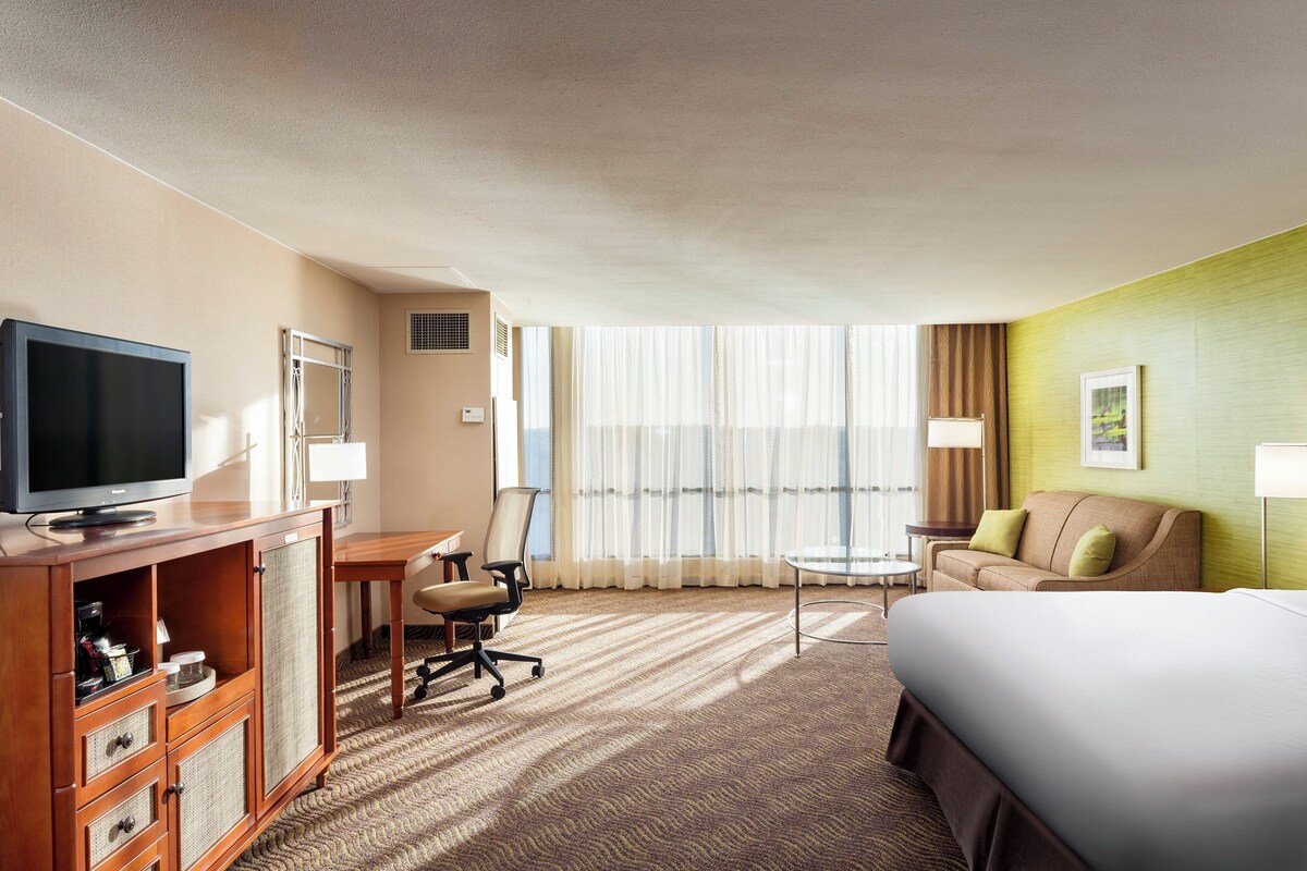 Quarto de hotel com uma cama grande, uma mesa com cadeira, televisão e um sofá.