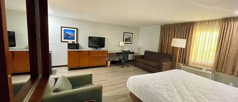 Quarto de hotel com cama, escrivaninha com computador, televisão, sofá e poltrona.