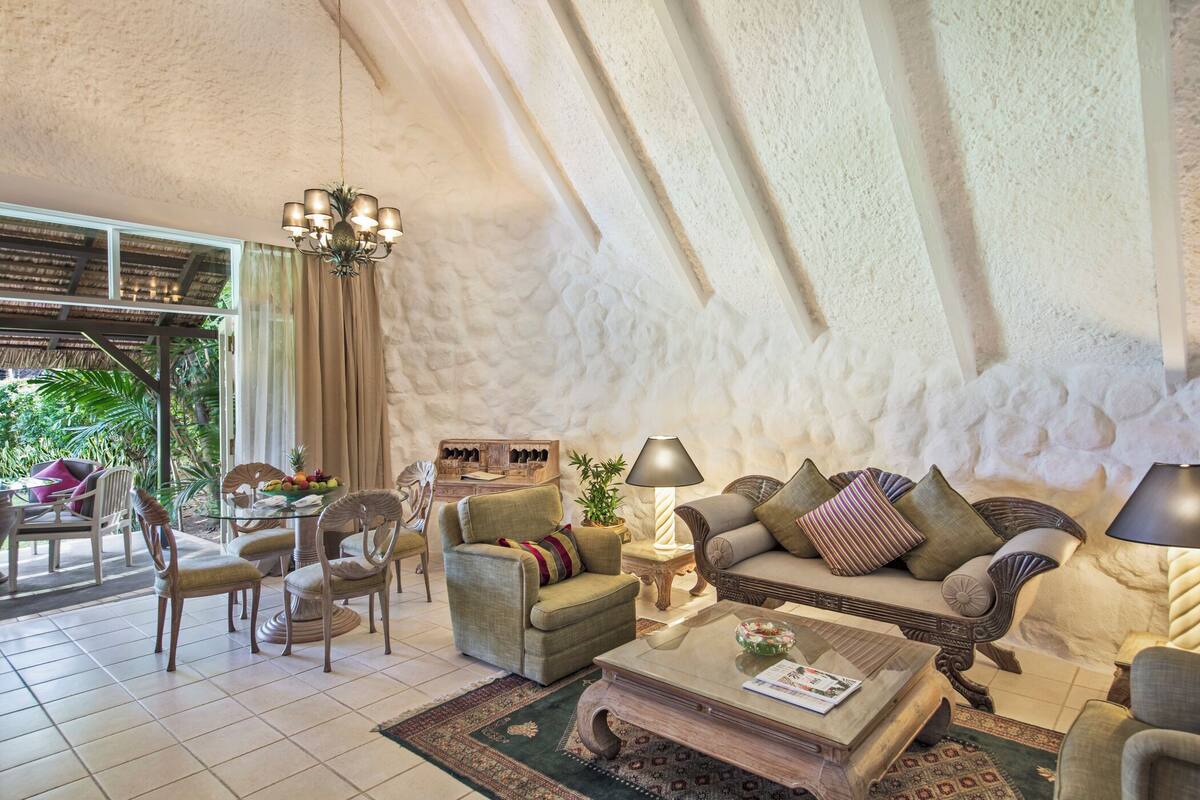 Uma sala de estar espaçosa, com teto alto, área de jantar com mesa de vidro e vista para o exterior.