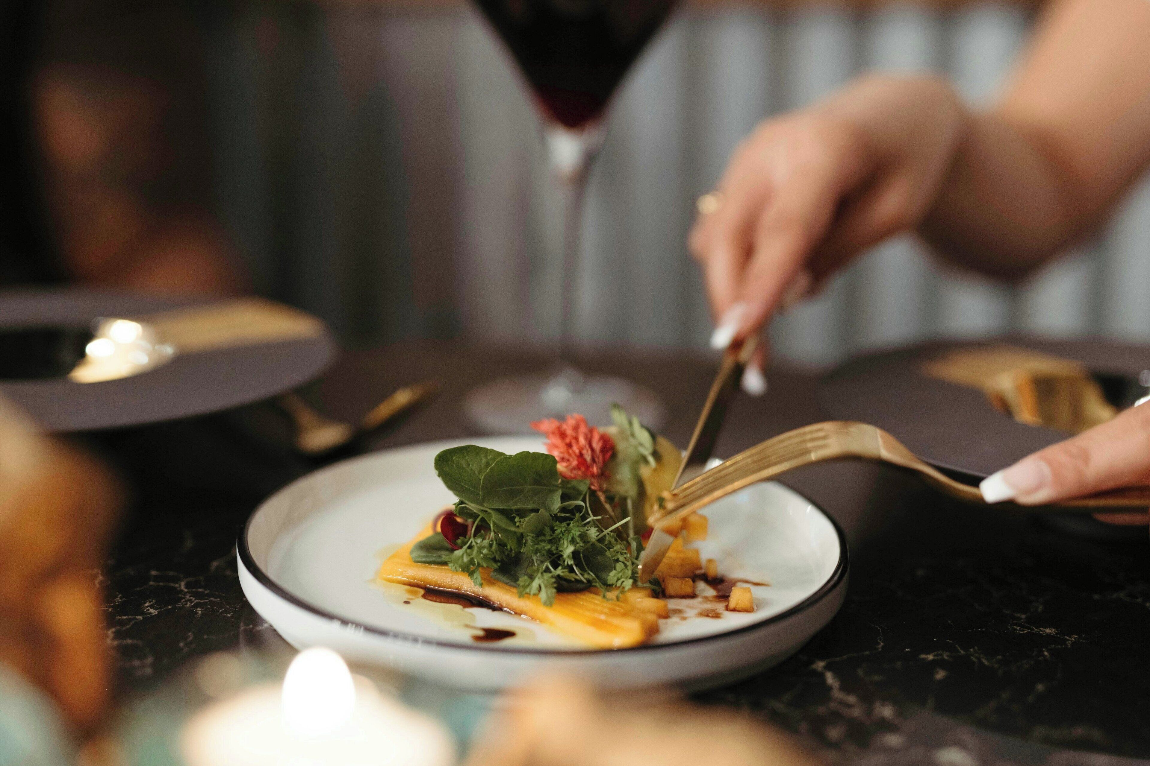 Um close-up de um prato gourmet em uma travessa, com um garfo, acompanhado de um copo de vinho tinto.