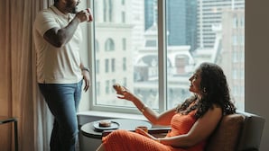 Um homem e uma mulher num quarto com uma janela grande que dá para uma paisagem urbana.