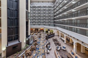 Um saguão de hotel em vários níveis, com um espaço central aberto, áreas de estar e uma mesa de recepção.