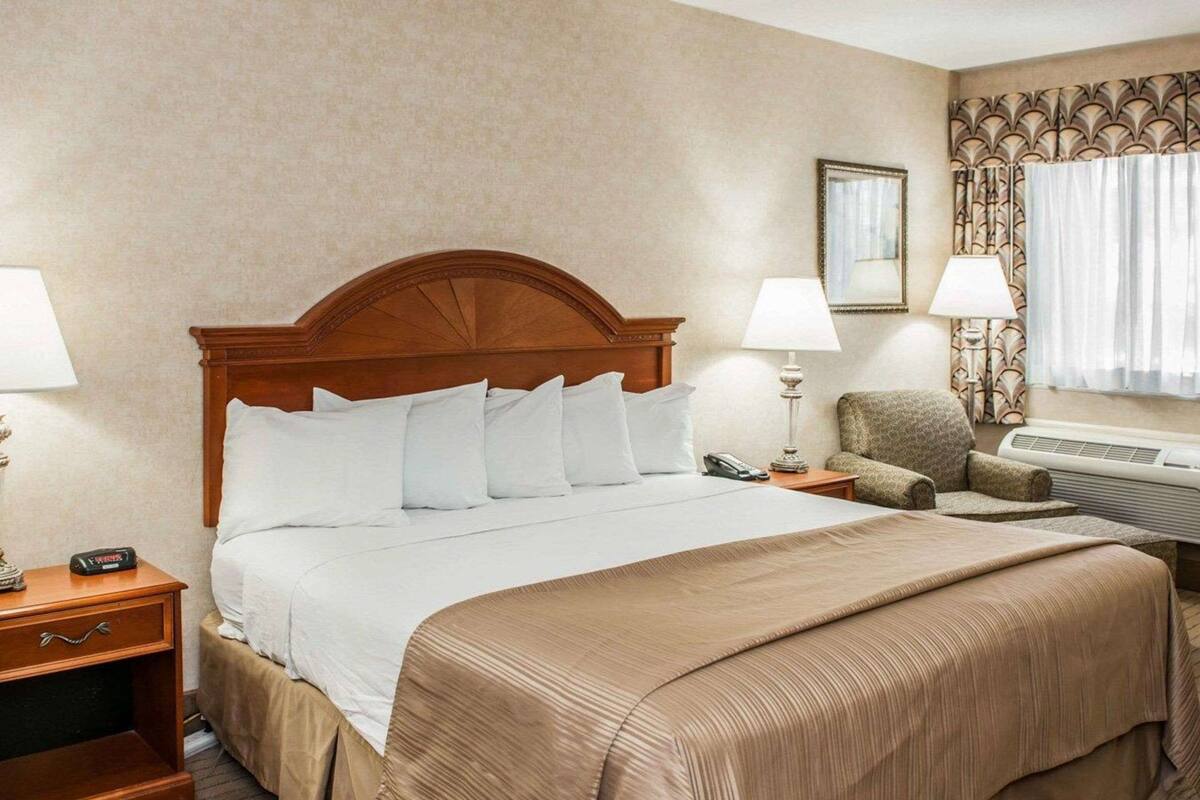 Quarto de hotel com uma cama grande, duas mesas de cabeceira, uma cadeira, uma escrivaninha e uma janela com cortinas.