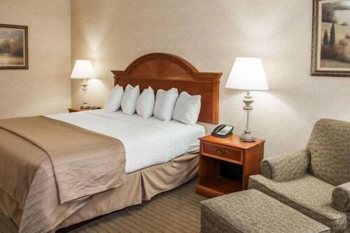 Quarto de hotel com cama, abajures, telefone, cadeira e um quadro na parede.