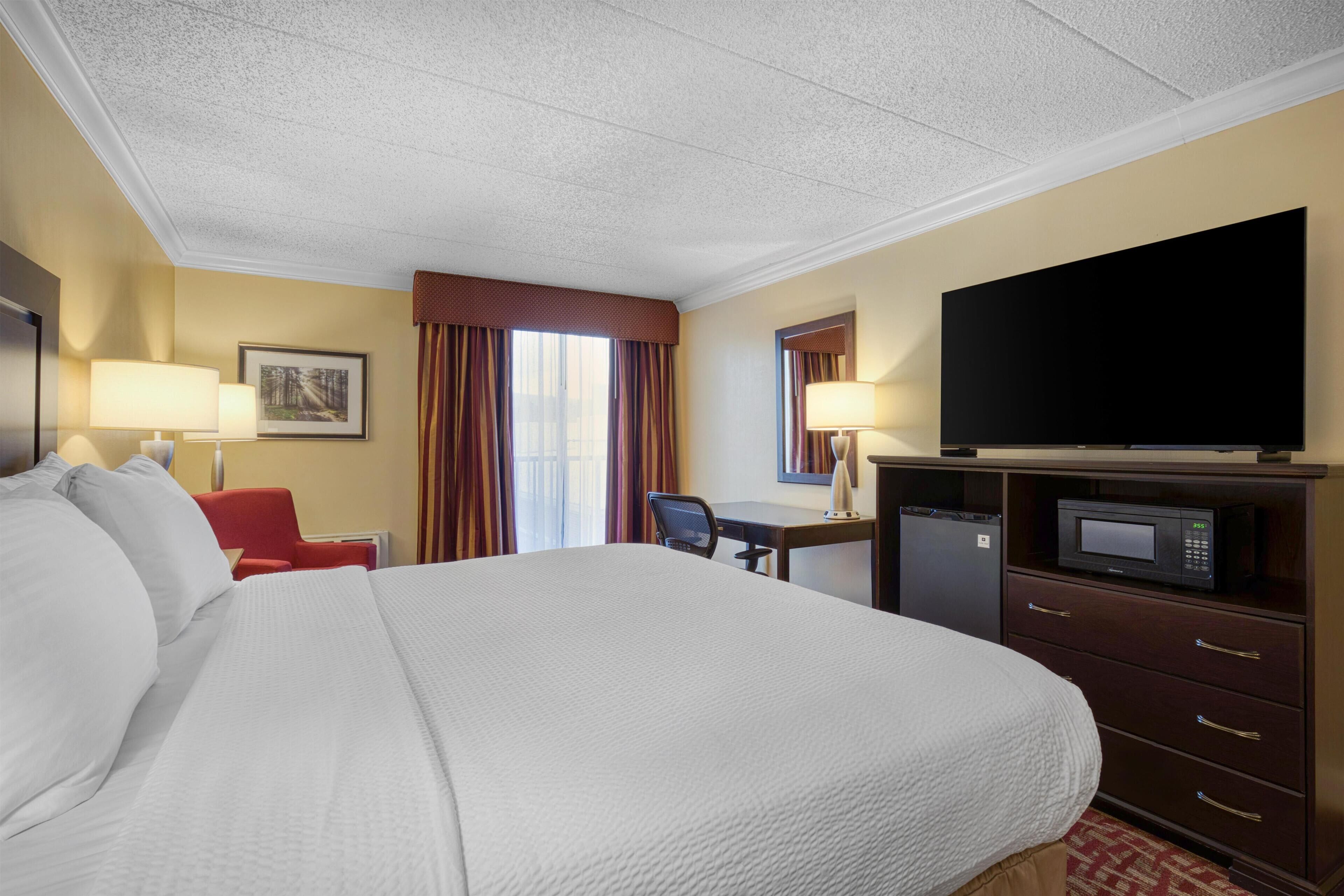 Quarto de hotel com uma cama grande, uma escrivaninha com computador, televisão e micro-ondas.