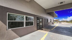 Um edifício com uma janela grande, uma porta e estacionamento.