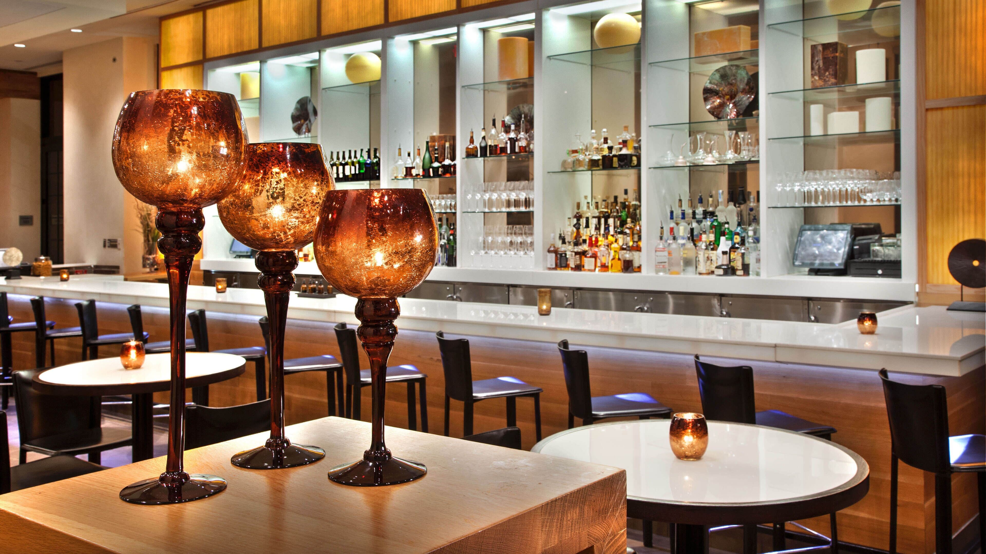 Uma área de bar com mesas redondas, banquetas e castiçais decorativos.