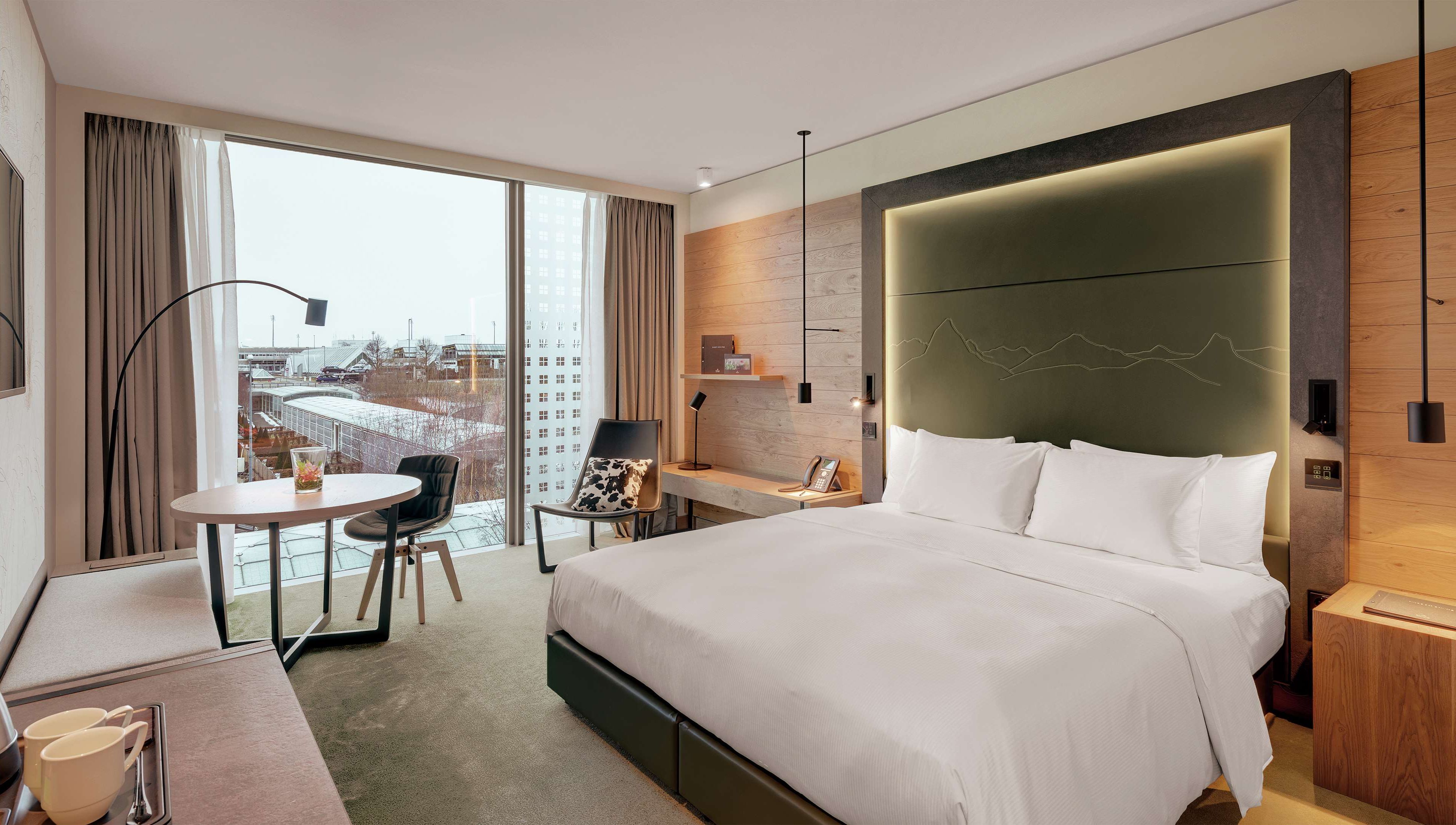Quarto de hotel com uma cama grande, escrivaninha, cadeira e vista para a cidade.