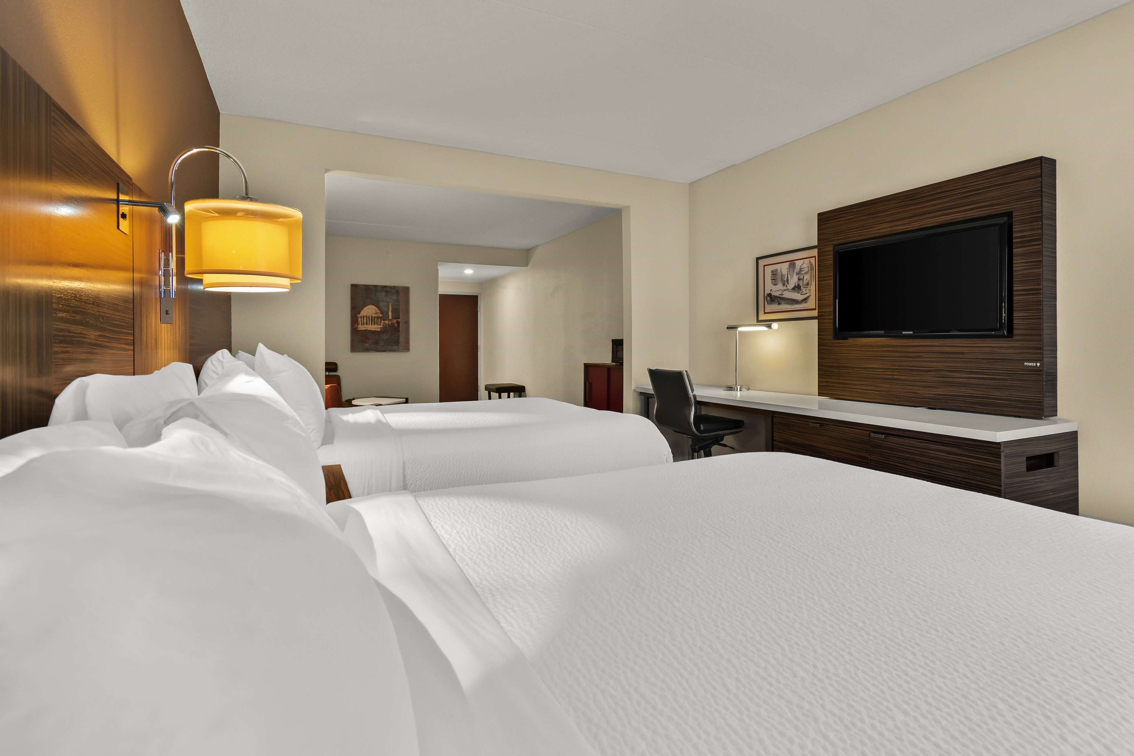 Quarto de hotel com duas camas, uma escrivaninha, uma televisão e um abajur.