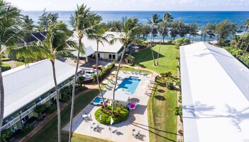 Vista aérea de um resort com piscina, palmeiras e vista para o oceano.