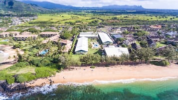 Vista aérea de um resort à beira-mar, com vários edifícios, uma praia e montanhas ao fundo.