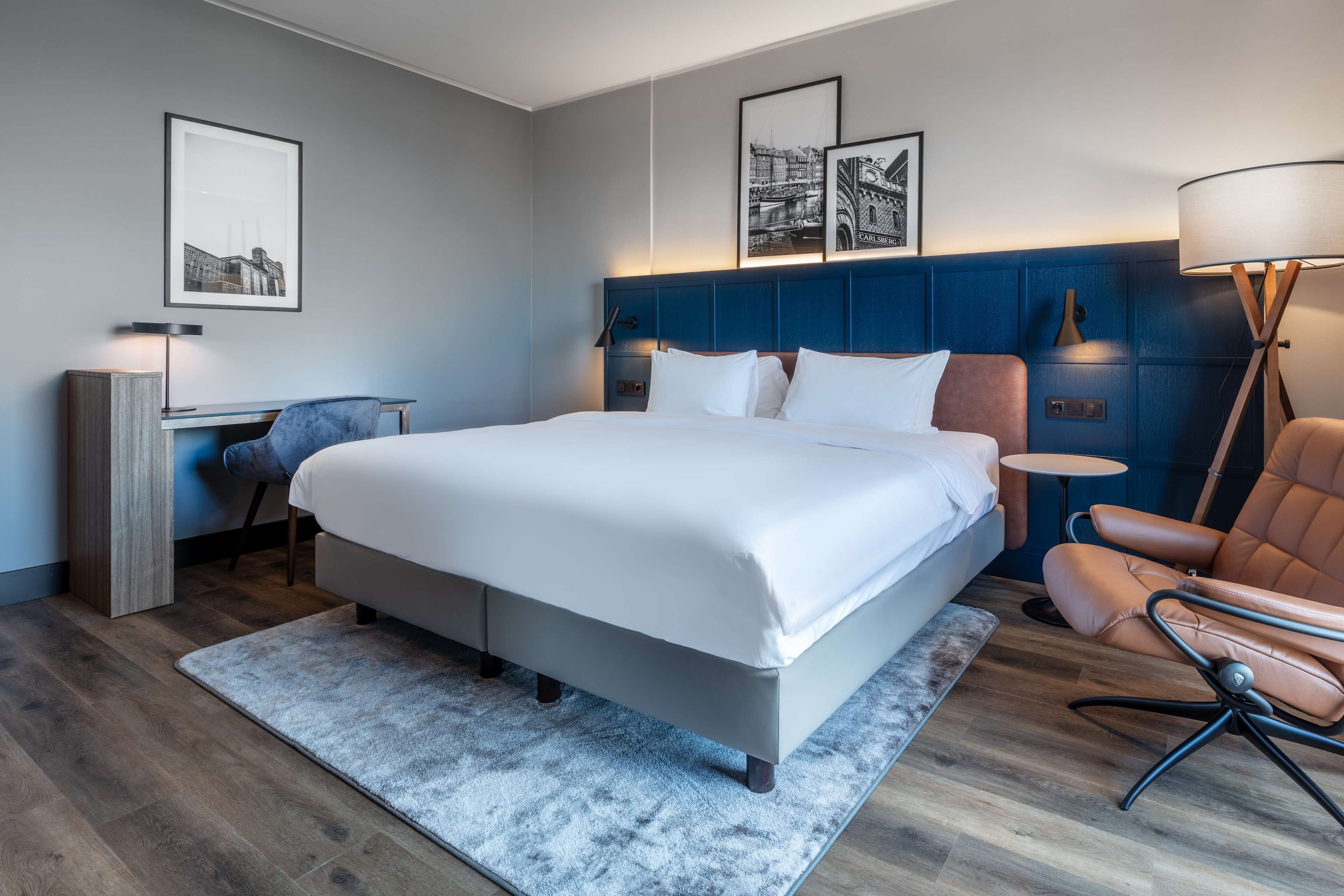 Quarto de hotel moderno com uma cama grande, uma escrivaninha, uma cadeira e um abajur.