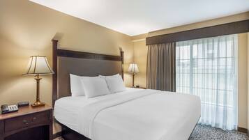 Quarto de hotel com uma cama grande, duas mesas de cabeceira com luminárias, um telefone e uma janela com cortinas.