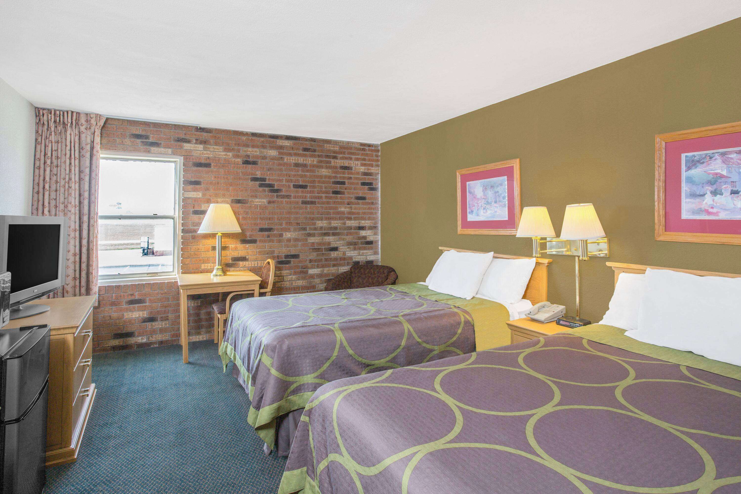 Quarto de hotel com duas camas, uma escrivaninha, uma cadeira, uma televisão e uma janela com cortinas.