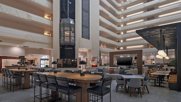 Um amplo saguão de hotel com diversas áreas de refeição, um espaço central para sentar e uma grande tela de televisão.