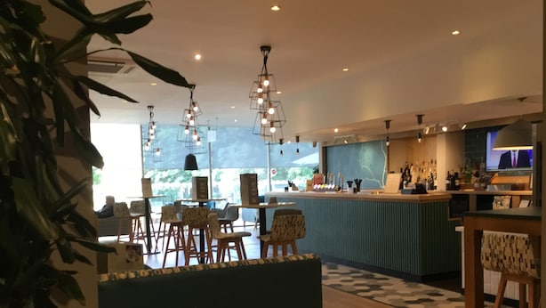 Uma área de bar moderna com balcão, banquetas e luminárias pendentes.