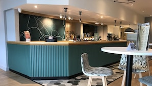Uma área de bar moderna com balcão verde, um banquinho de madeira e uma mesa com cardápio.