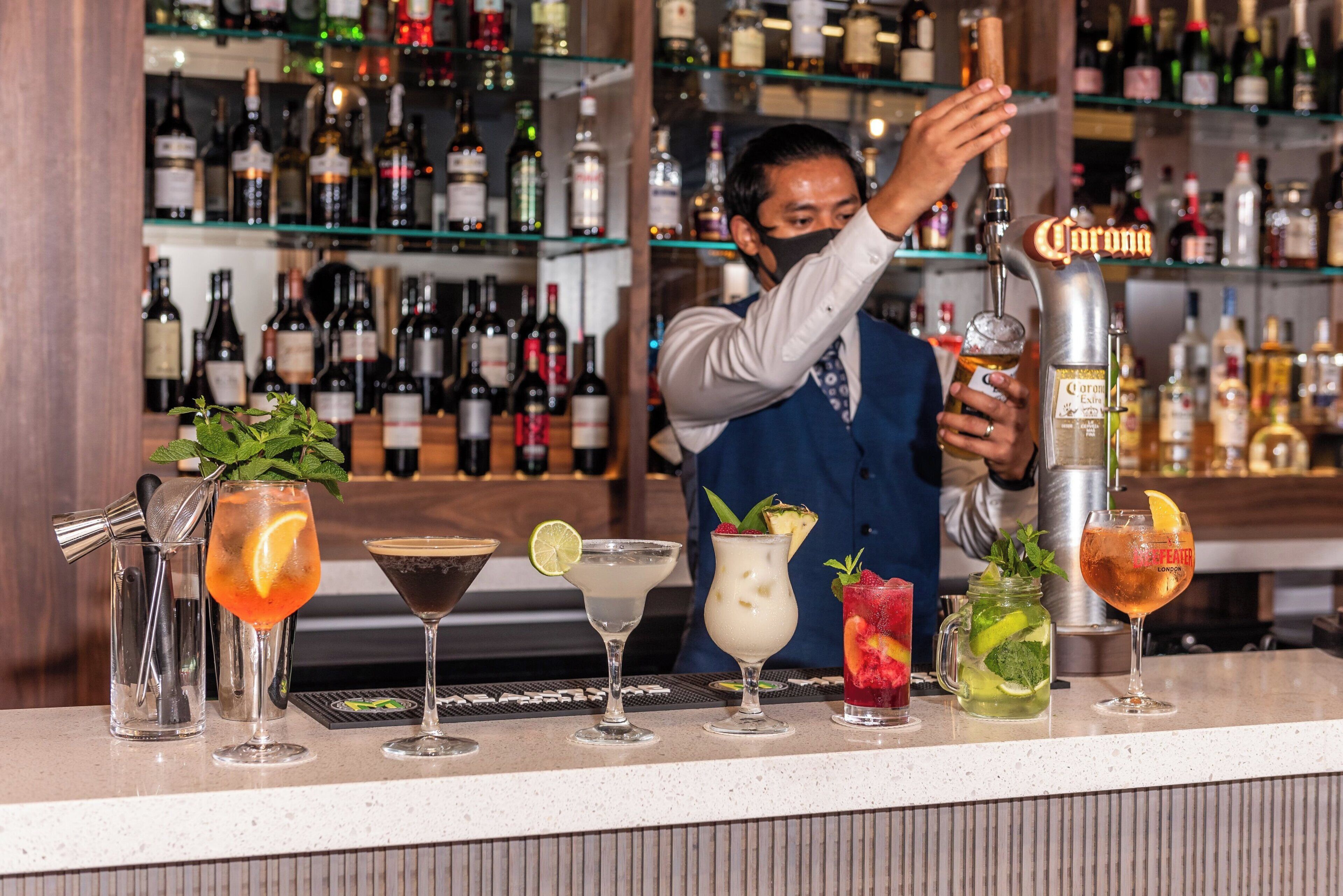 Bar com diversos coquetéis e um bartender preparando bebidas.