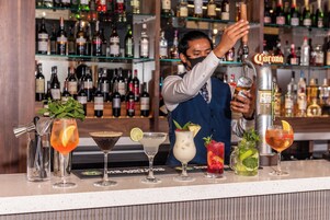 Bar com diversos coquetéis e um bartender preparando bebidas.
