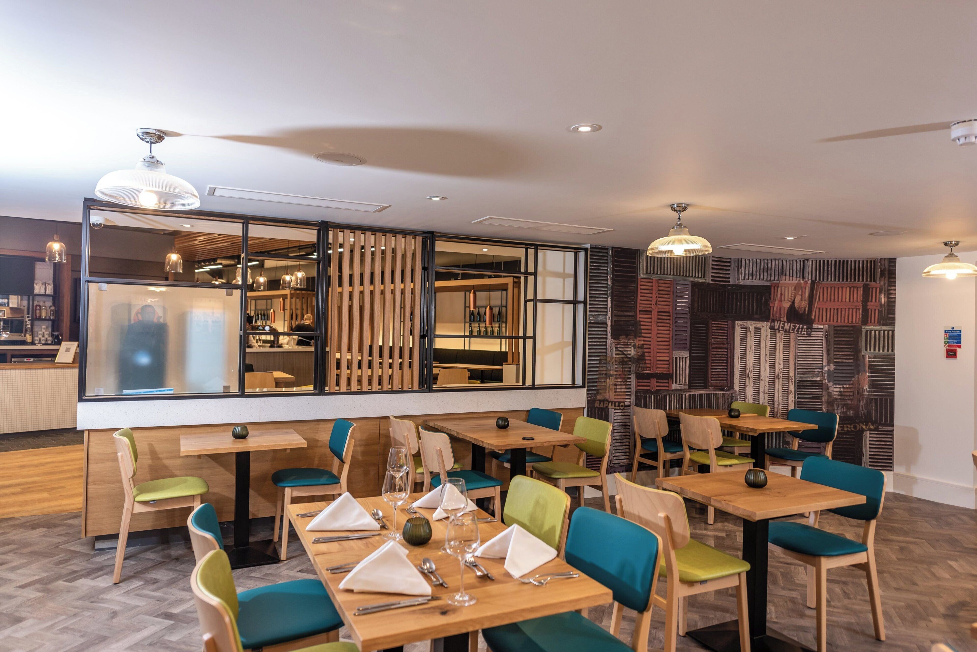 Um restaurante com mesas e cadeiras de madeira, um espaço de bar e vista para a cozinha.