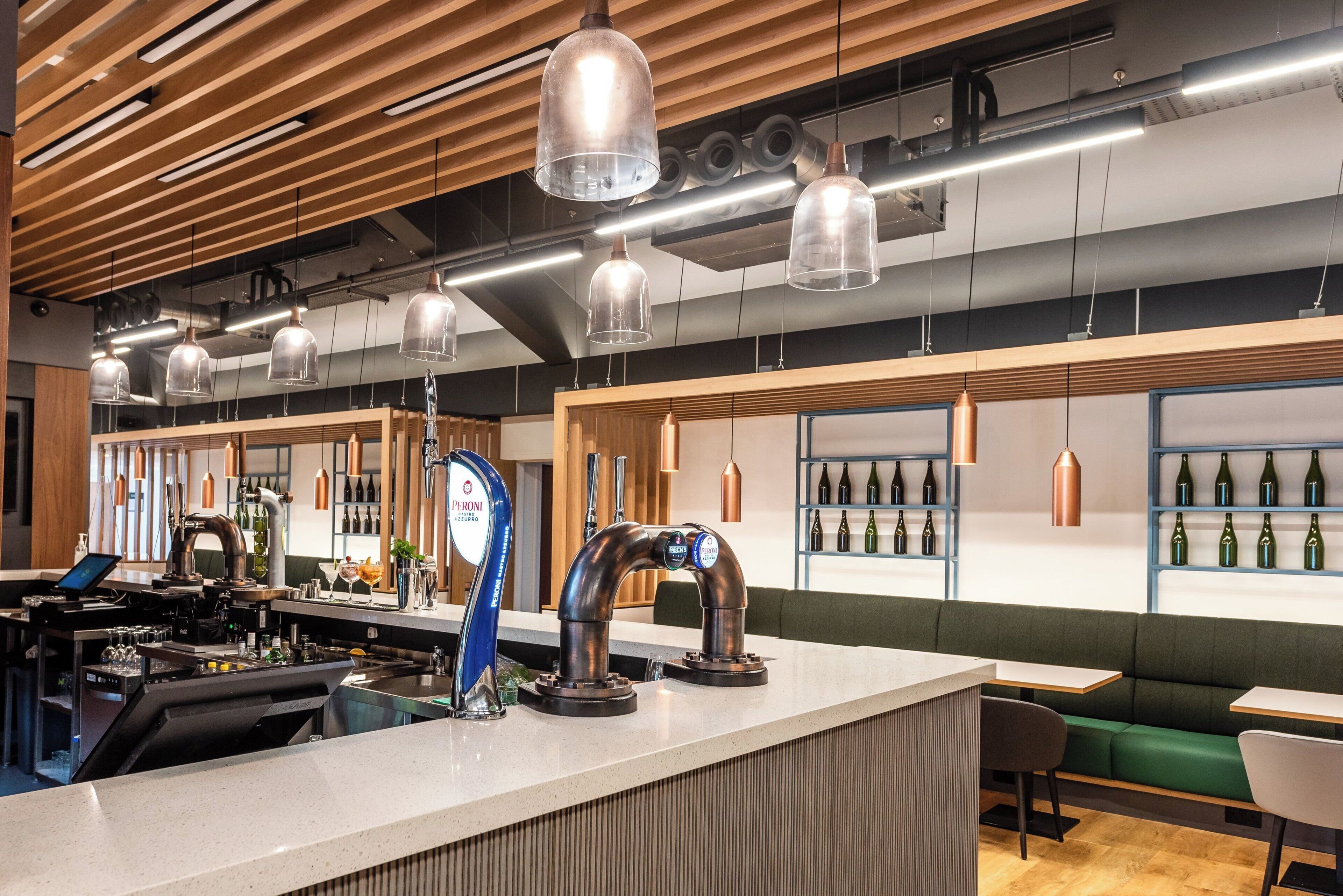 Uma área de bar com design moderno, incluindo um balcão com torneira de cerveja e um barman robótico.