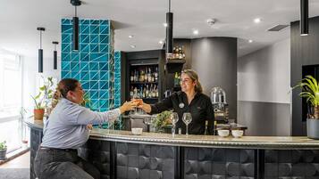 Uma área de bar com design moderno, com balcão, banquetas e uma estante com garrafas.