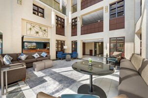 Um hall amplo com teto alto, várias áreas de estar e uma mesa redonda central.