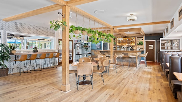 Restaurante com pisos de madeira, cadeiras de vime e plantas penduradas.