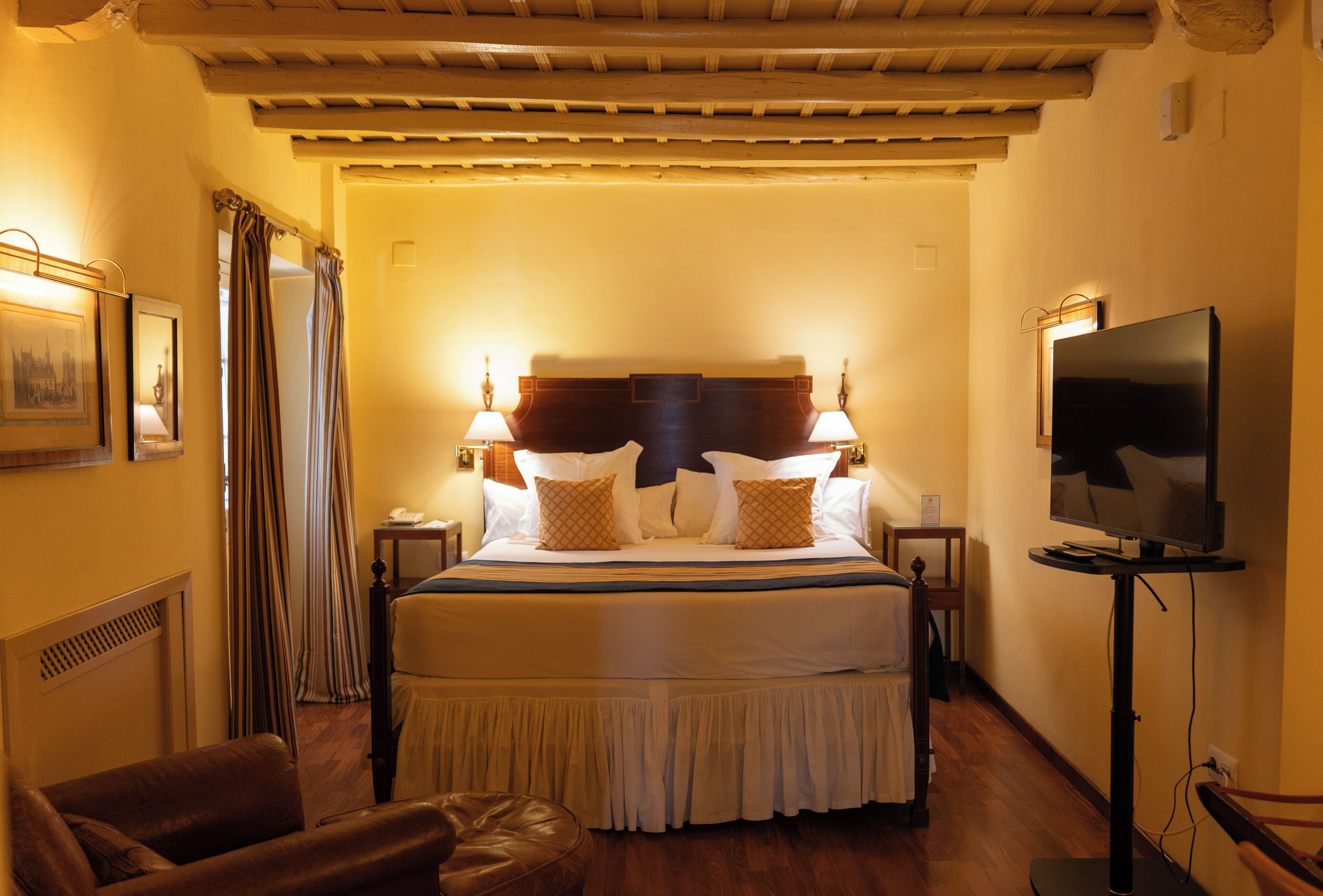 Quarto de hotel com uma cama grande, televisão e teto de madeira.