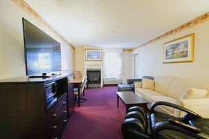 Quarto de hotel com televisão, lareira, sofá, escrivaninha e uma cadeira.