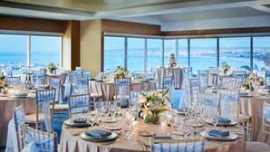 Uma área de refeições com mesas redondas preparadas para um evento formal, com cadeiras de vidro transparente e louças elaboradas.