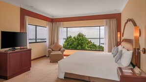 Quarto de hotel com uma cama grande, uma televisão, uma cadeira e vista para o exterior.