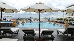 Uma área à beira da piscina com espreguiçadeiras, guarda-sóis e estátuas decorativas.