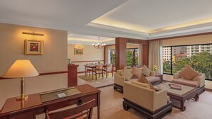 Quarto de hotel com escrivaninha, dois sofás, área de jantar e vista para o verde.