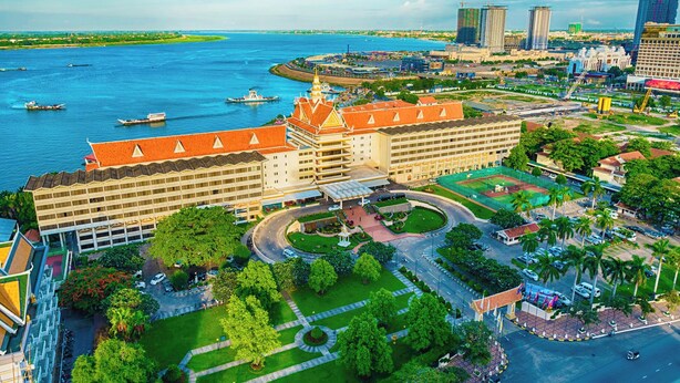 Um hotel grande com um pátio central, rodeado por vegetação exuberante e vista para a orla.