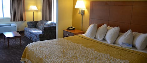 Quarto de hotel com uma cama grande, um sofá, uma escrivaninha e uma luminária.