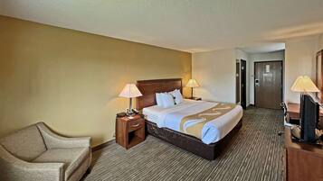 Quarto de hotel com uma cama, duas mesas de cabeceira com abajures, uma cadeira, uma televisão e uma porta que dá para outro quarto.