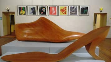 Uma galeria de arte moderna com uma escultura de madeira e pinturas abstratas na parede.