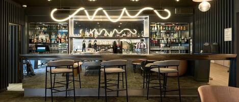 Uma área de bar com banquetas, um balcão com garrafas e um tapete estampado.