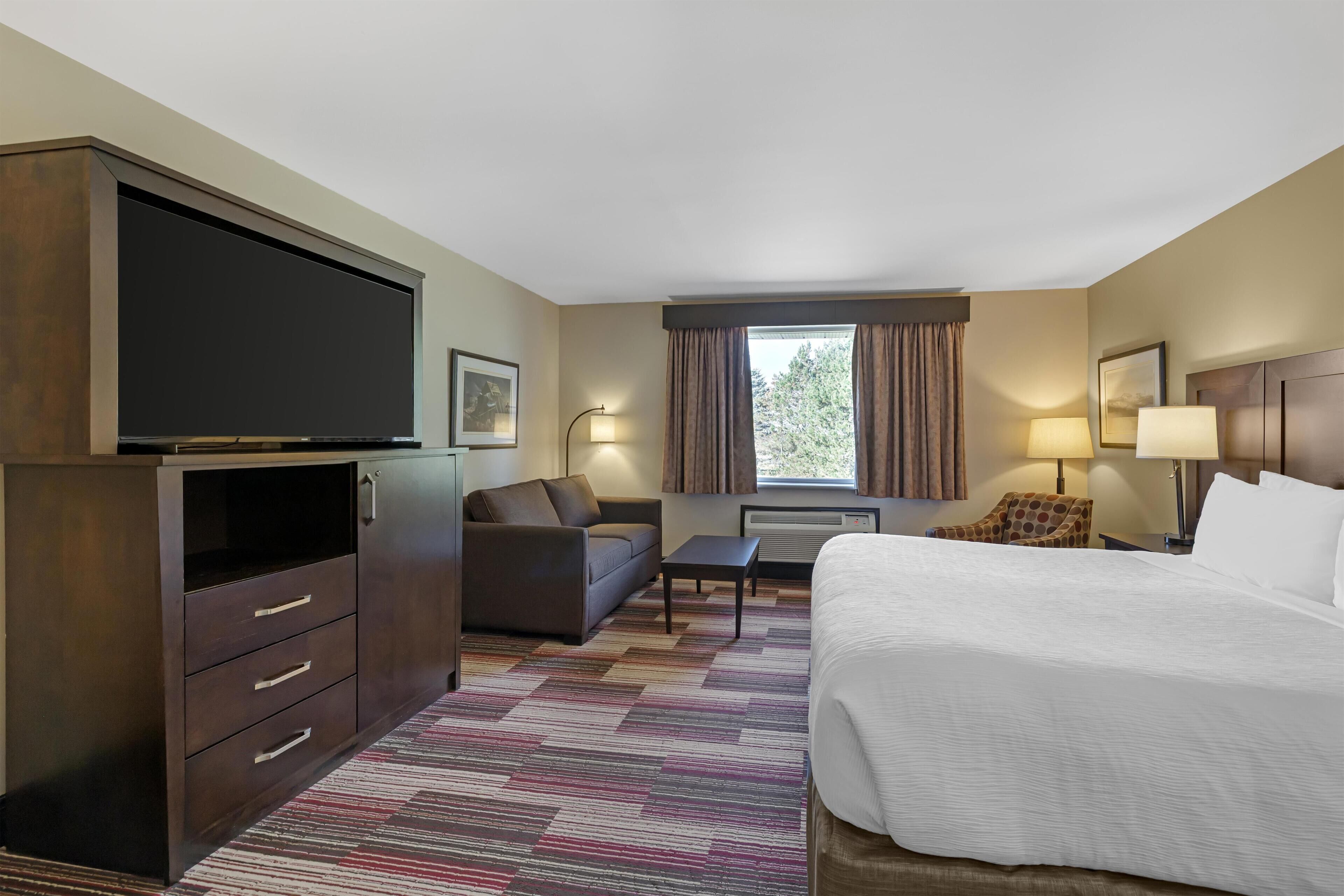 Quarto de hotel com cama, sofá, escrivaninha, televisão e guarda-roupa.