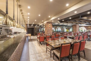 Um restaurante espaçoso com várias mesas e cadeiras, um balcão comprido com painel de aço inoxidável e uma parede de tijolos com uma grande janela ao fundo.